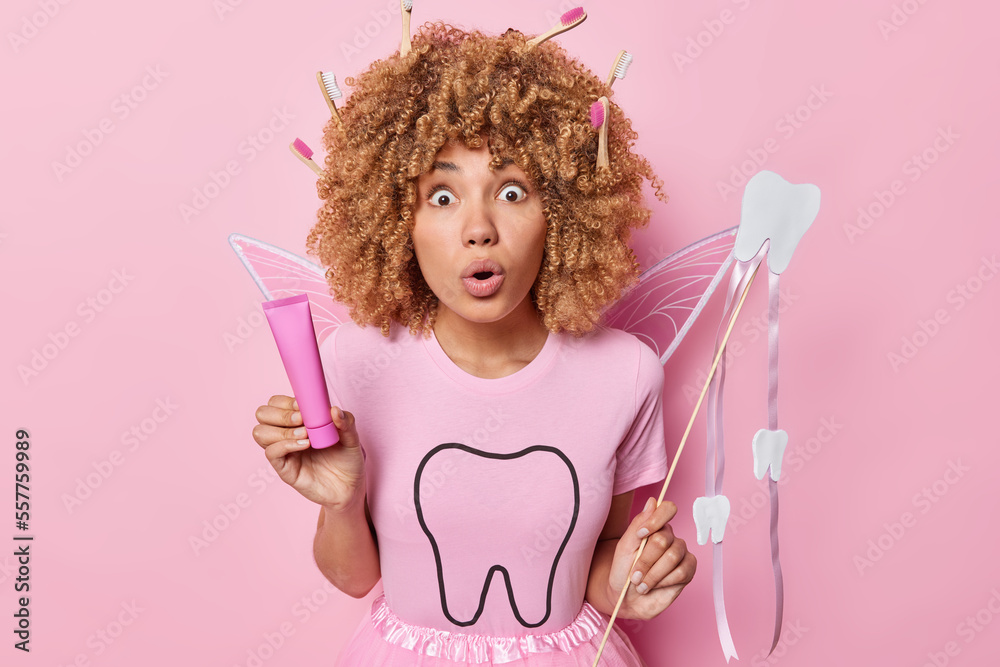 Waist up shot of shocked curly haired female tooth fairy holds ...