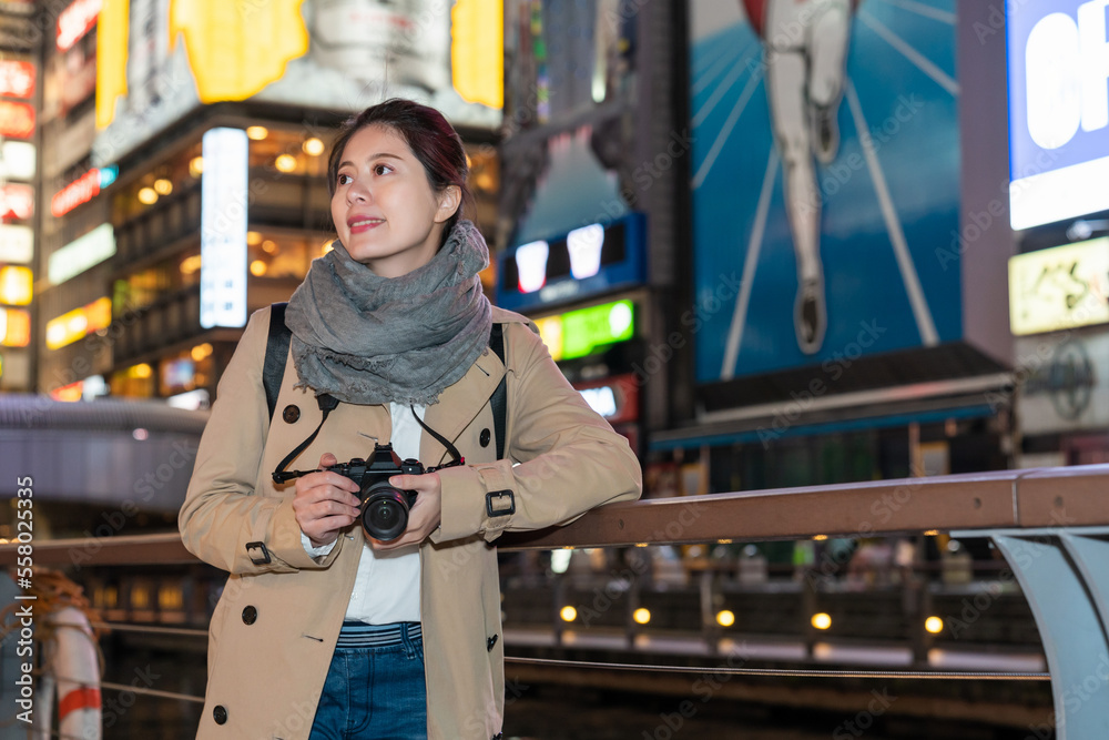 cheerful Asian Japanese woman visitor holding camera and admiring night ...
