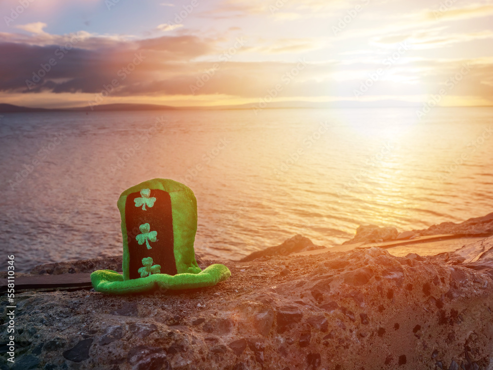 Small green hat with shamrock in focus. Stunning sunset scene in the ...