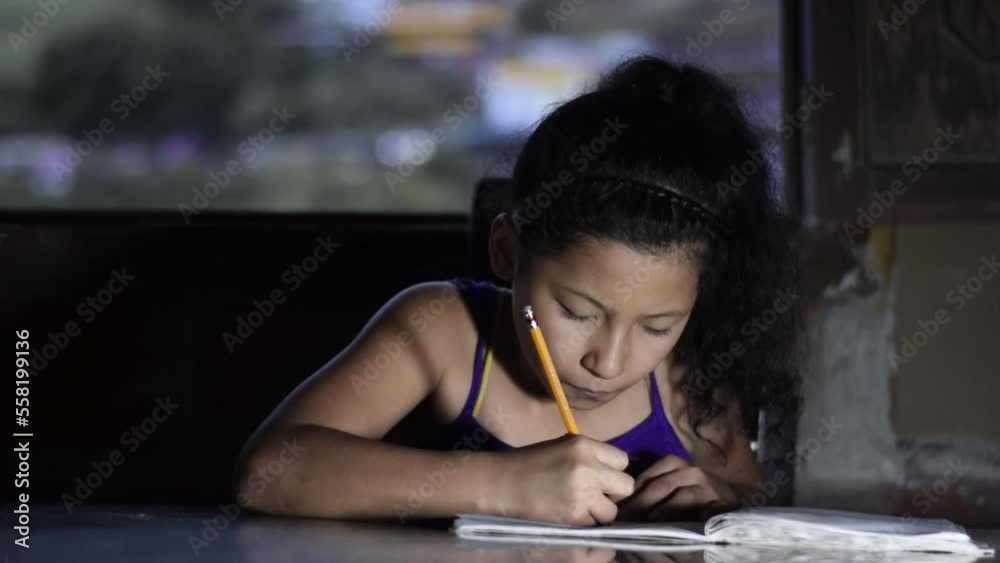 poor little latina girl, doing her homework with very little light in ...
