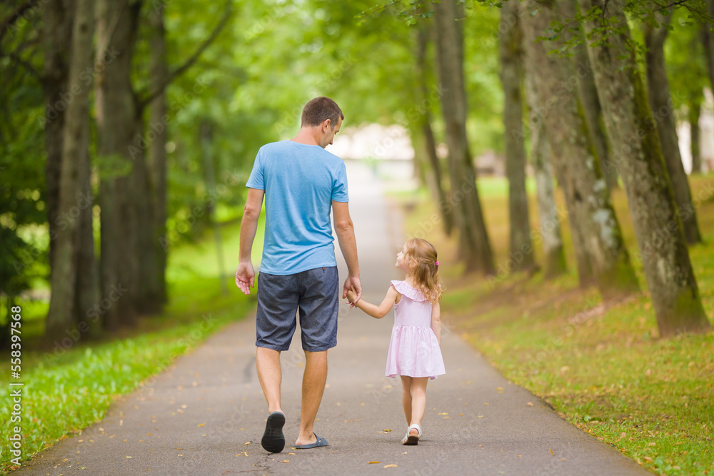 Little daughter and young adult father speaking and walking on sidewalk ...