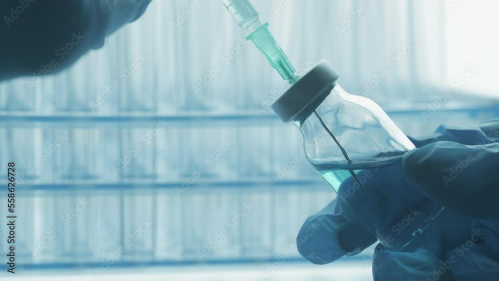 A doctor is drawing up vaccine from phial bottle and filling syringe ...