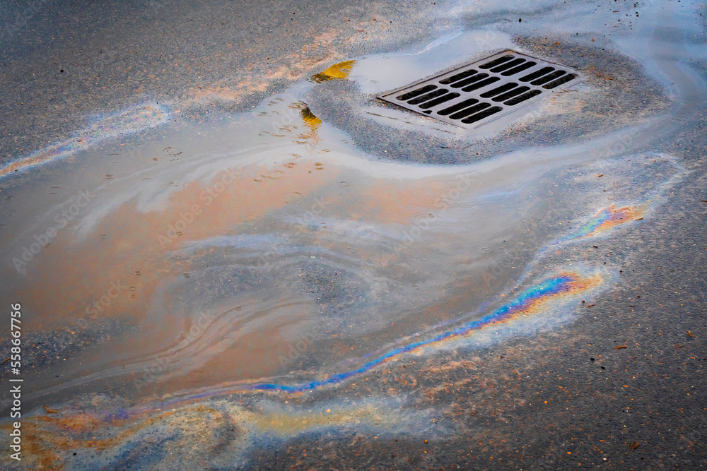 Oil slick on the asphalt road background drains into the storm drain ...