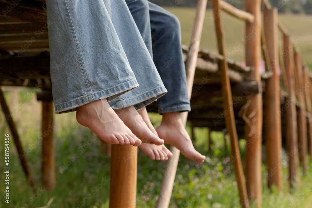Detail of woman and teenager sitting on the border of a wooden bridge ...