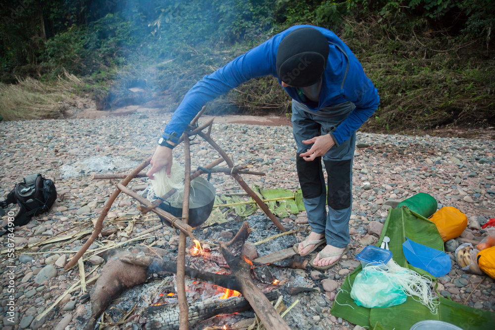Man cooking over campfire while camping on the Nam Ou River in Phou Den ...