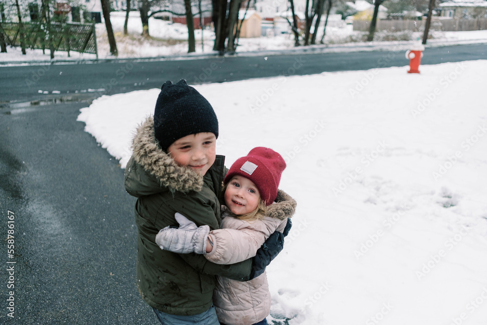 Siblings hugging each other in their driveway while playing in snow ...