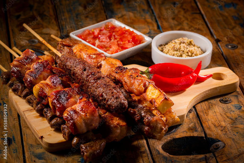 Foto de Espetinhos de churrasco em tábua de madeira com acompanhamentos ...