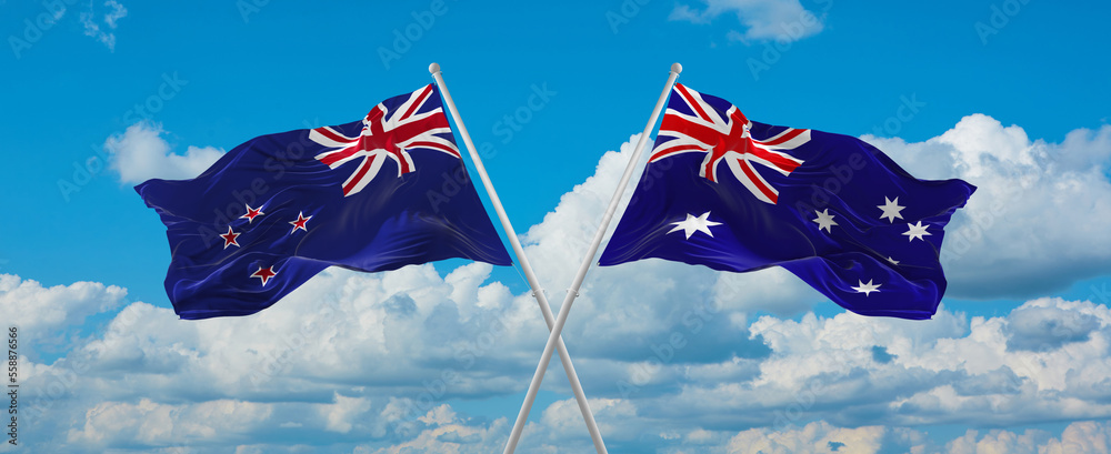 two crossed flags Australia and New Zealand waving in wind at cloudy sky. Concept of ...