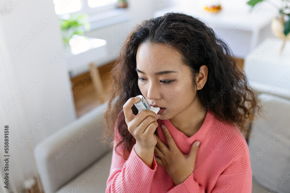 Asian woman using inhaler while suffering from asthma at home. Young ...