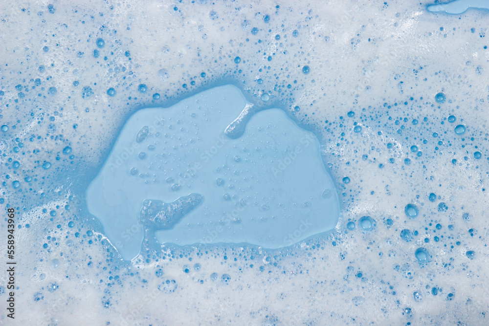 Soap suds on water on a blue background with copy space. Foam texture ...