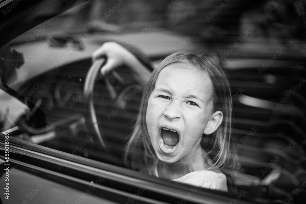 A little girl is sitting behind the wheel of a car, messing around and ...