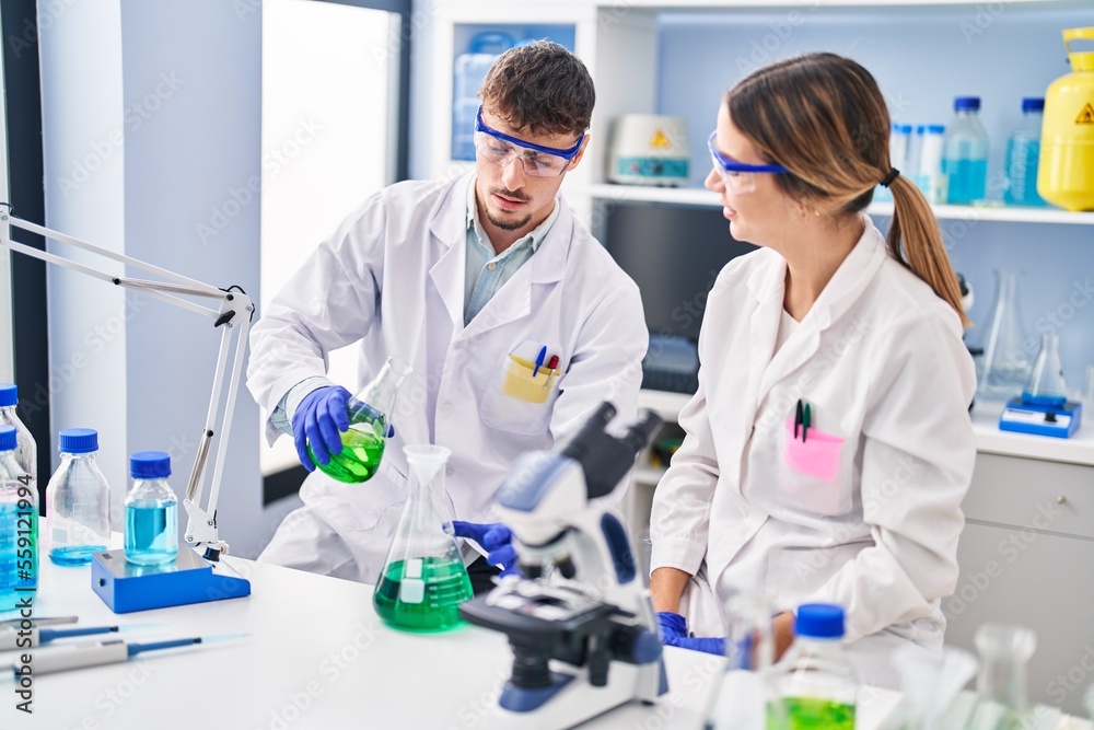 Young man and woman scientists workers measuring liquid at laboratory ...