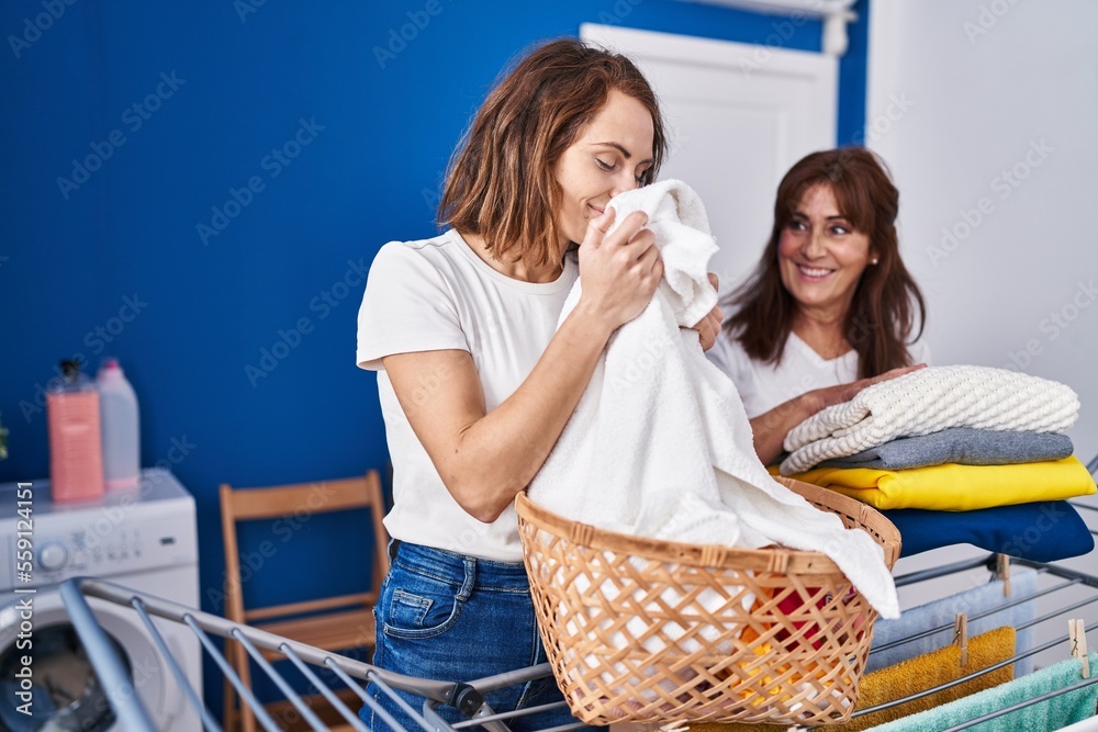 Two women mother and daughter smelling clean clothes at laundry room ...
