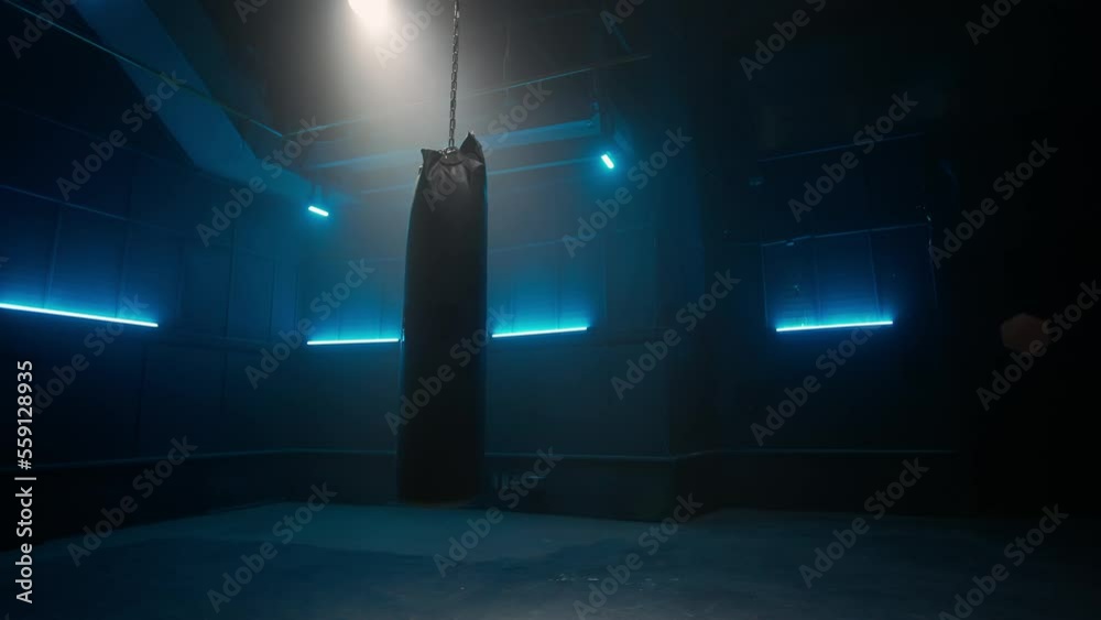 Long black punchbag hanging and swinging from chain in dark empty gym ...