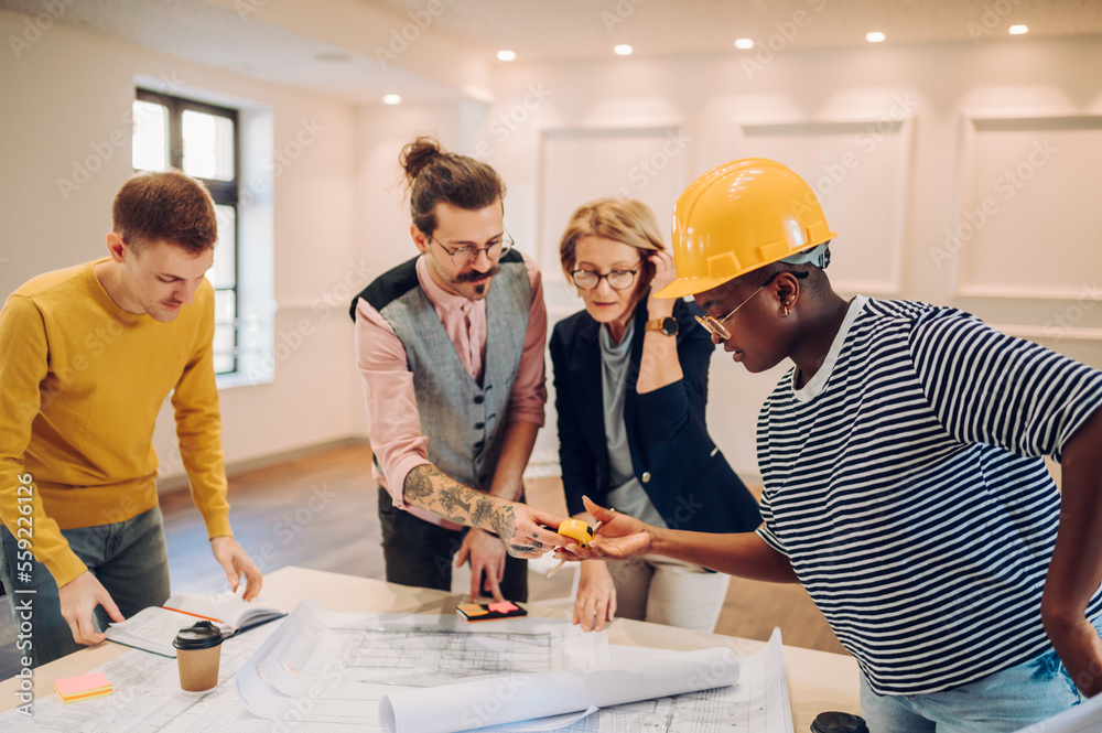 Multiracial team of architects having a meeting while using blueprints ...