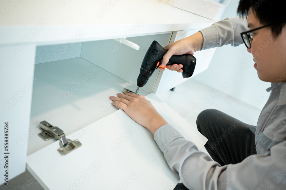 Asian male furniture assembler using electric drill screwdriver on ...