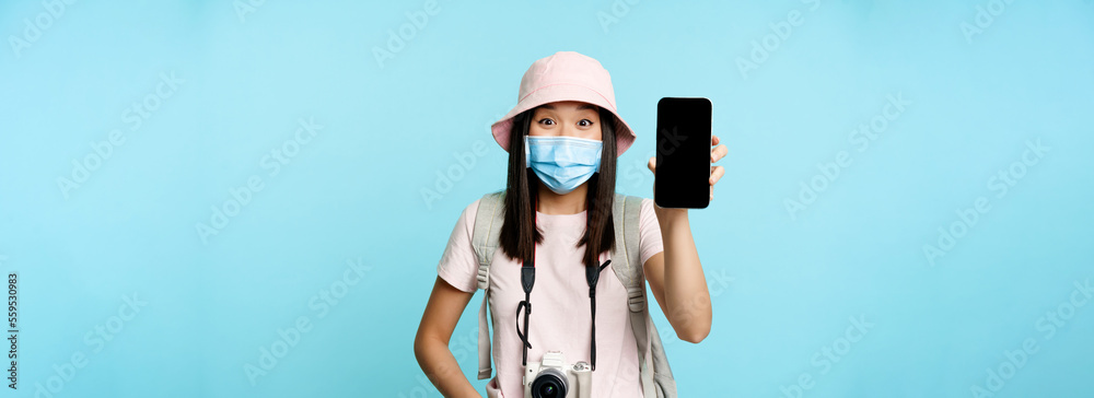 Enthusiastic young asian woman in medical face mask, showing mobile ...