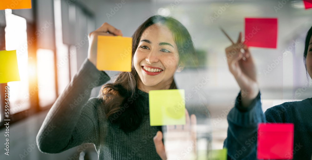 Young businesswoman creative team using post it notes in glass wall to ...