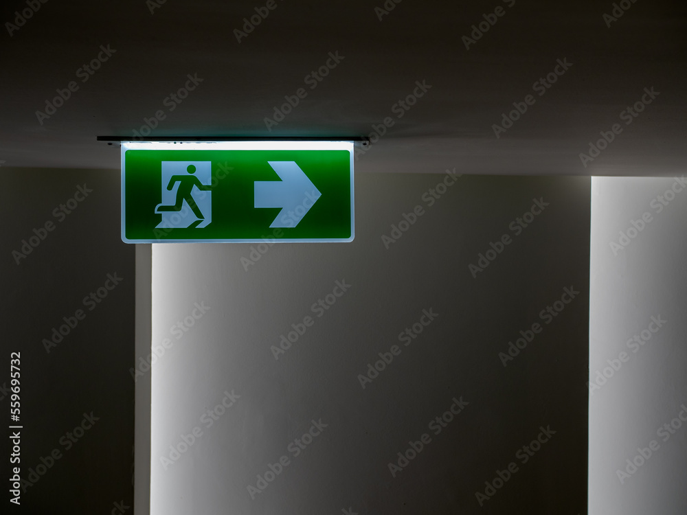 Green fire escape sign hang on the ceiling in the dark building ...