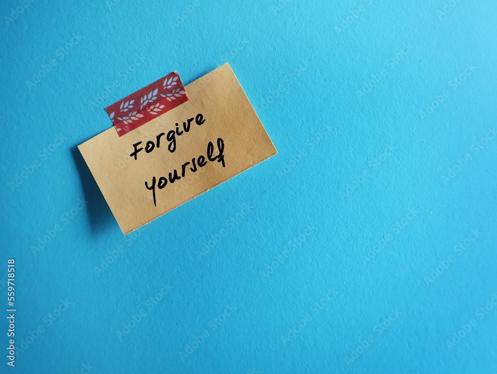 Stick note on blue copy space background with handwritten text FORGIVE ...