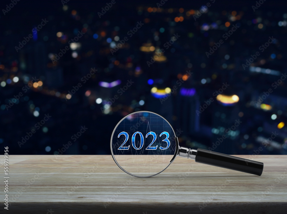 Foto de Magnifying glass with 2023 text and financial graph on wooden ...