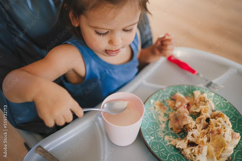 Cute baby girl eating food by herself, sitting on high chair. Caucasian ...