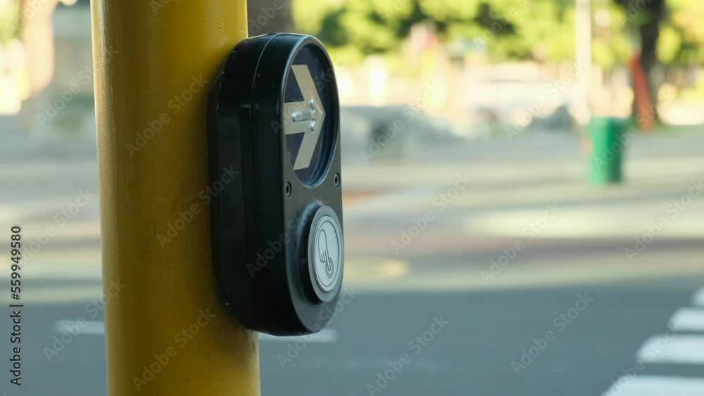 Female pedestrian presses a traffic light button to cross the road. The ...