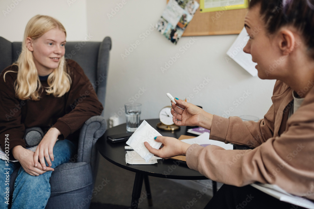 School nurse giving tampon and sanitary pad to female student sitting ...