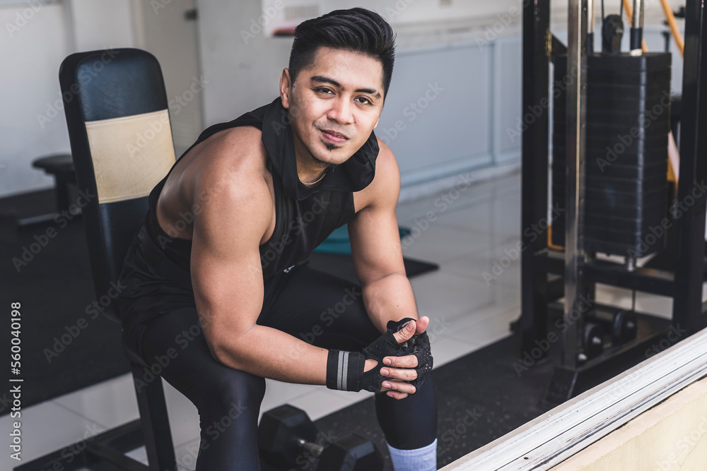 A confident asian man smirking while sitting on an incline bench at the ...