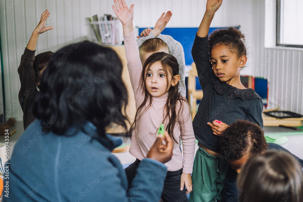 Female teacher asking questions and students raising hand to answer at ...