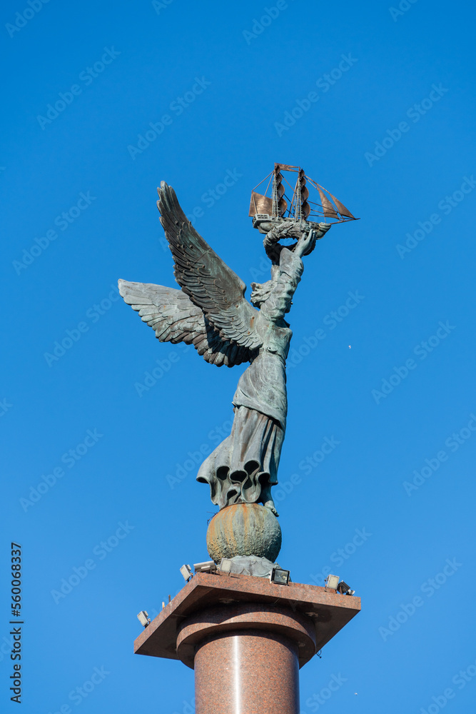 Angel with wings stands on ball at top of column with sailboat in ...