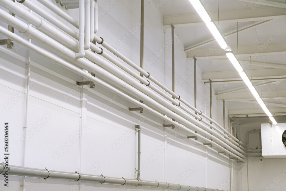 Lines of plastic pipelines fixed along the wall in industrial building ...