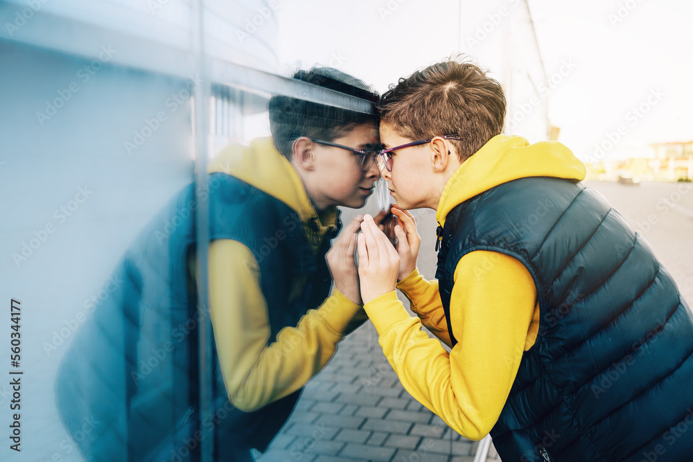 sad teenager boy with glasses looks closely at his own smiling ...