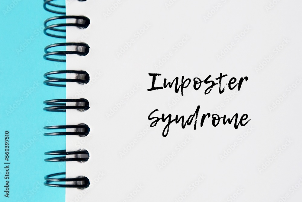 Notebook on blue background with handwritten text IMPOSTER SYNDROME ...