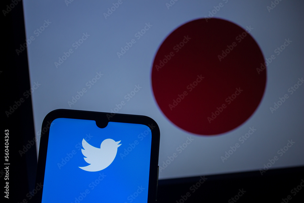 Twitter logo displayed on the smartphone screen. Blurry flag of Japan ...