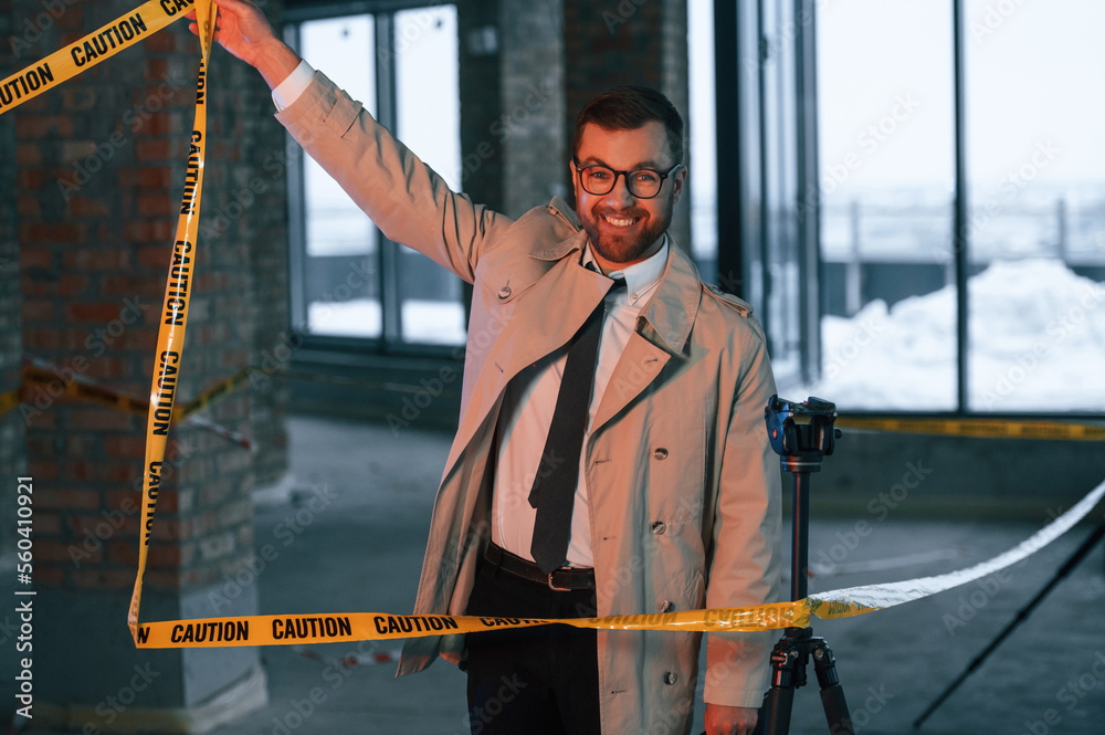 Positive detective in coat is holding caution police tape and smiling ...