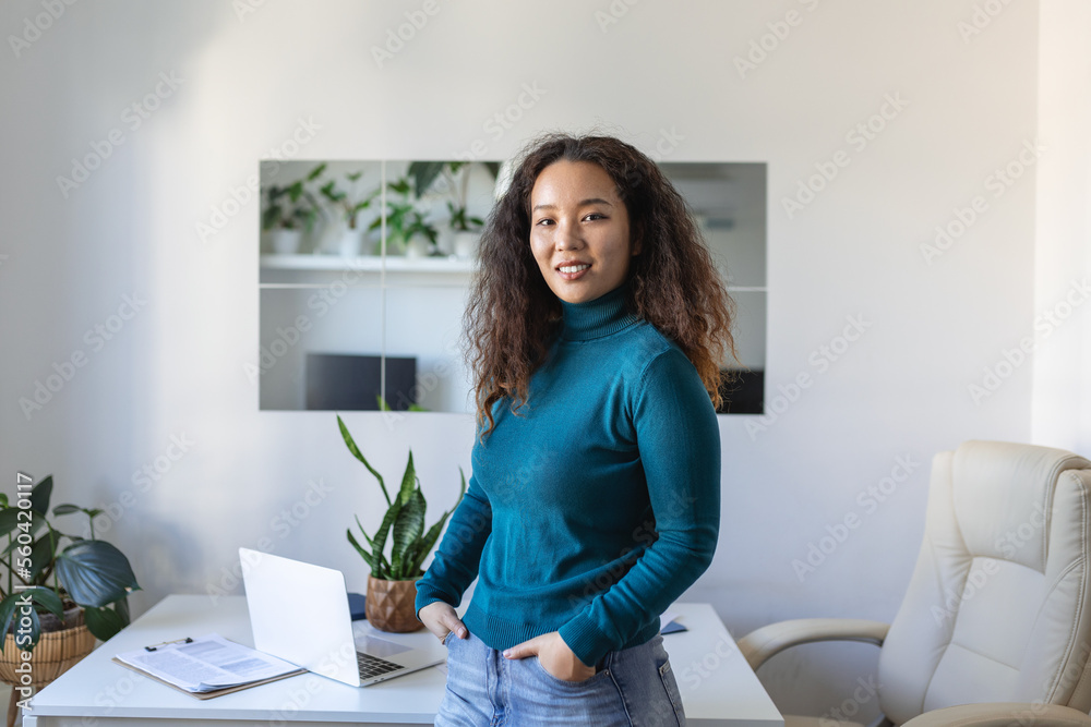 Smiling young Asian female employee stand at desk in office look in ...