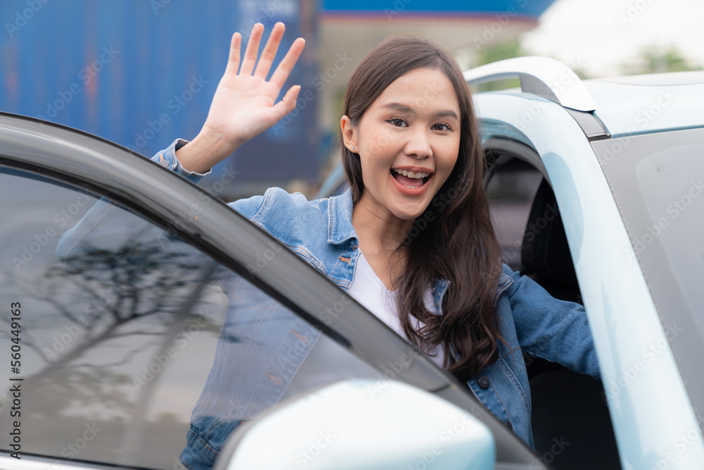 Asia woman standing at car raise hand up with smile at EV car at ...