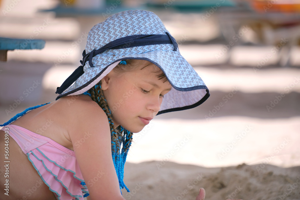 Pretty child girl in bikini swimsuit playing with sand in umbrella ...