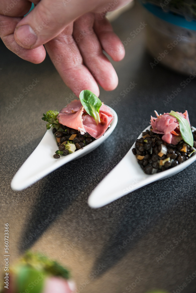 Cook preparing appetizer made of black gram and ham on spoons Stock ...