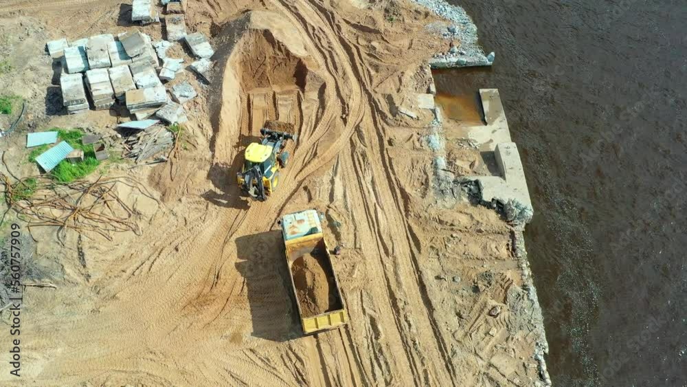 Tractor with a bucket in front loads the soil sand into the truck body ...