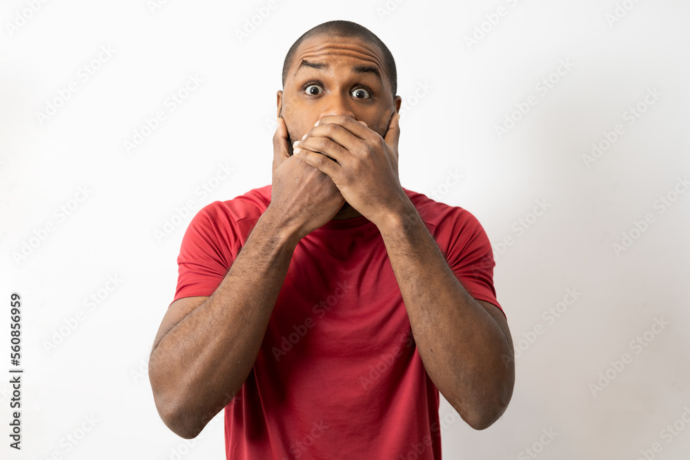 Shocked scared dark-skinned young man with shocked face covering mouth ...