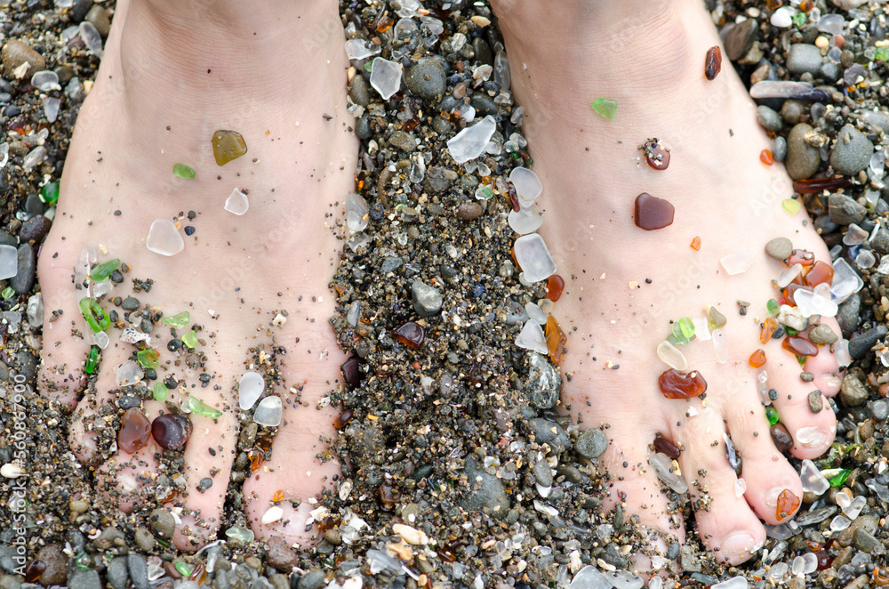 A mans feet are covered in glass from the handfuls of beach glass that ...