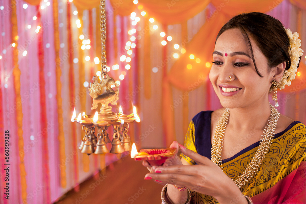 Beautiful young Indian female holding a diya and lighting up hanging ...