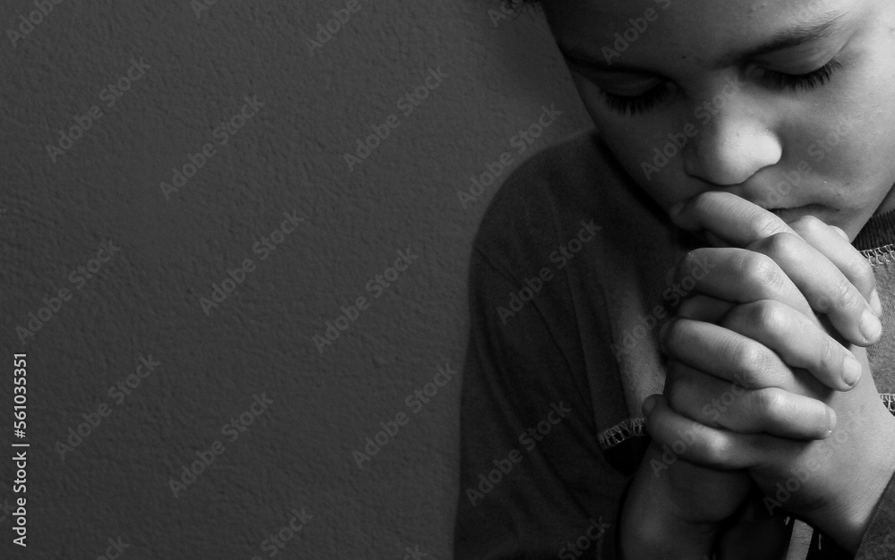 child praying to God with hands together on black background with ...