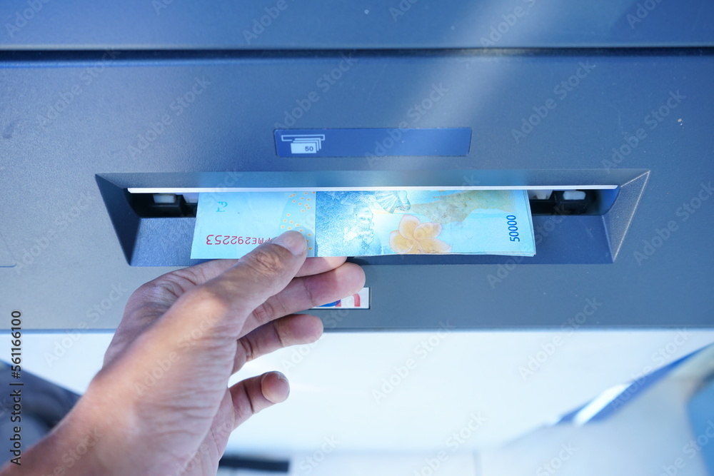 Asian man's hand is taking rupiah notes coming out of the ATM machine ...