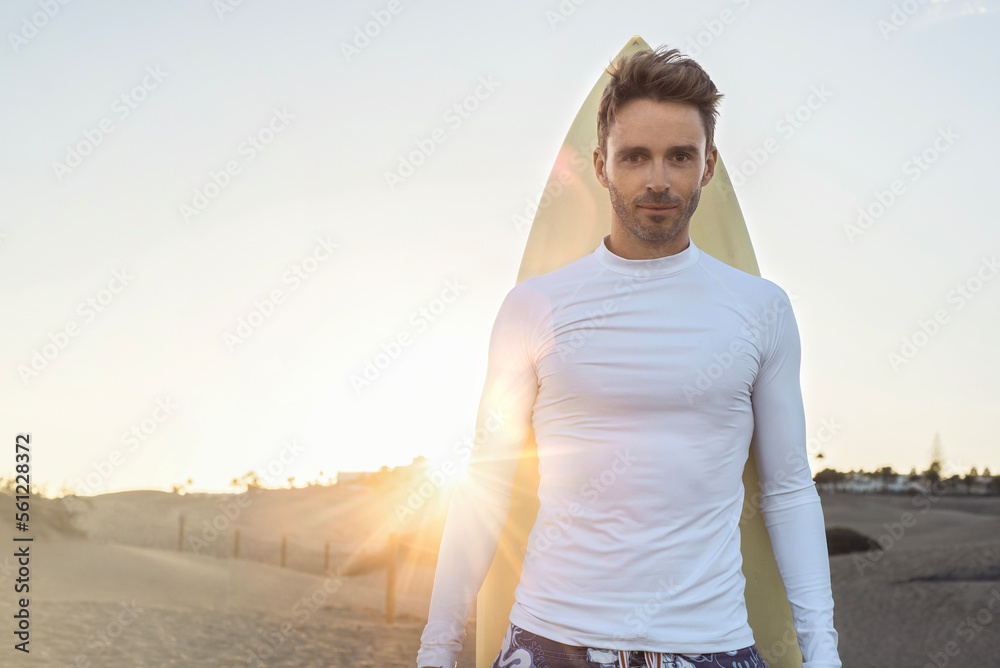 Young handsome surfer guy is standing next to his surfboard and wearing ...