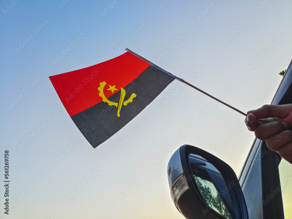 Boy waving Angola flag against the blue sky from the car window close ...