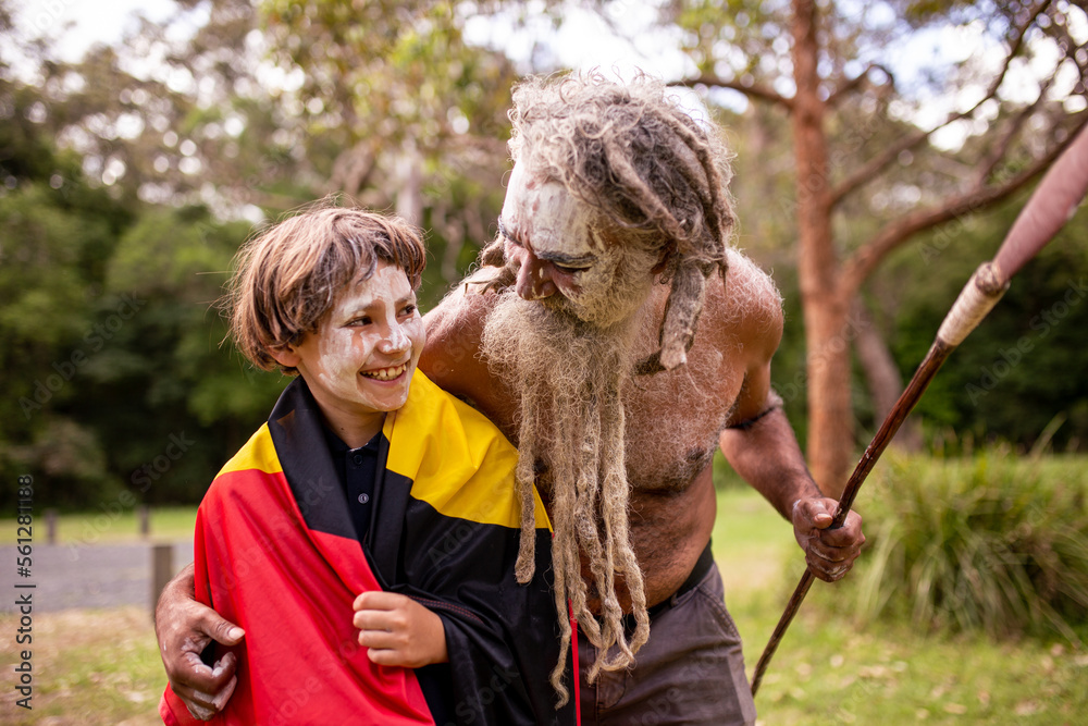 Young Aboriginal boy wearing the Aboriginal flag and being hugged by ...