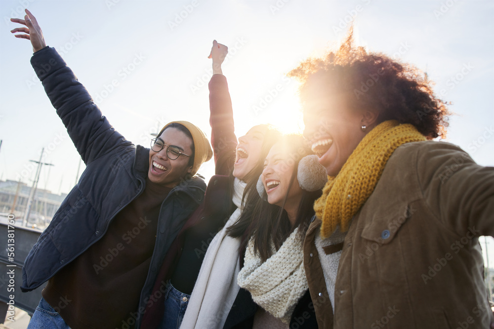 Side view of a group of excited young friends having fun together outdoor. Diverse people ...